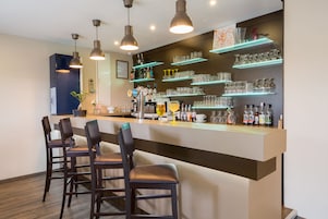 Uma área de bar moderna com balcão, banquetas e prateleiras cheias de copos e garrafas.