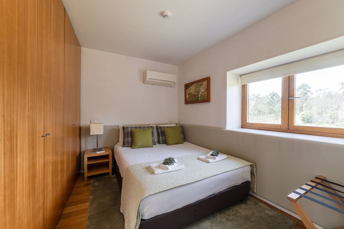 Quarto com cama, janela, guarda-roupa e mesa de cabeceira.