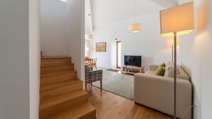 Uma sala de estar moderna com escada, sofá, televisão e área de refeições.