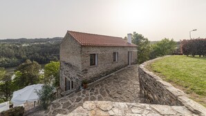 Um edifício de pedra com telhado de telhas vermelhas, uma escadaria de pedra que leva até ele, e vista para um rio e vegetação ao fundo.