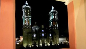 Fotografia emoldurada de um edifício histórico com duas torres imponentes, exposta numa parede com moldura branca e uma pequena luz iluminada abaixo.