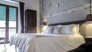 Quarto com cama grande, mesa de cabeceira, luminária, guarda-roupa e vista para o exterior através de uma porta.