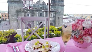 Uma mesa com toalha rosa, um prato de comida, um copo de bebida e um vaso de flores.