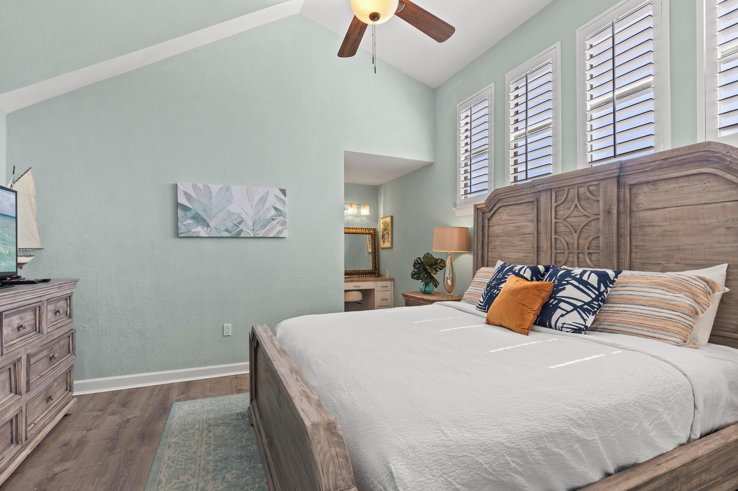Quarto com cama grande, cabeceira de madeira e ventoinha no teto.
