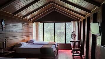 Quarto com paredes e teto de madeira, uma cama, uma cadeira, uma escrivaninha e uma televisão.