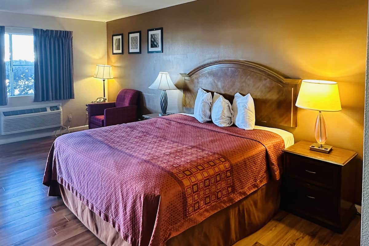 Quarto de hotel com uma cama grande, duas luminárias de cabeceira, uma cadeira e uma janela com cortinas.