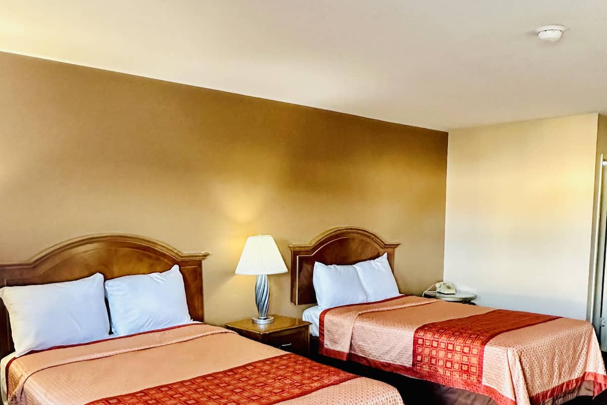 Quarto de hotel com duas camas, cada uma com cabeceira de madeira, luminária de cabeceira e telefone na mesa de apoio.