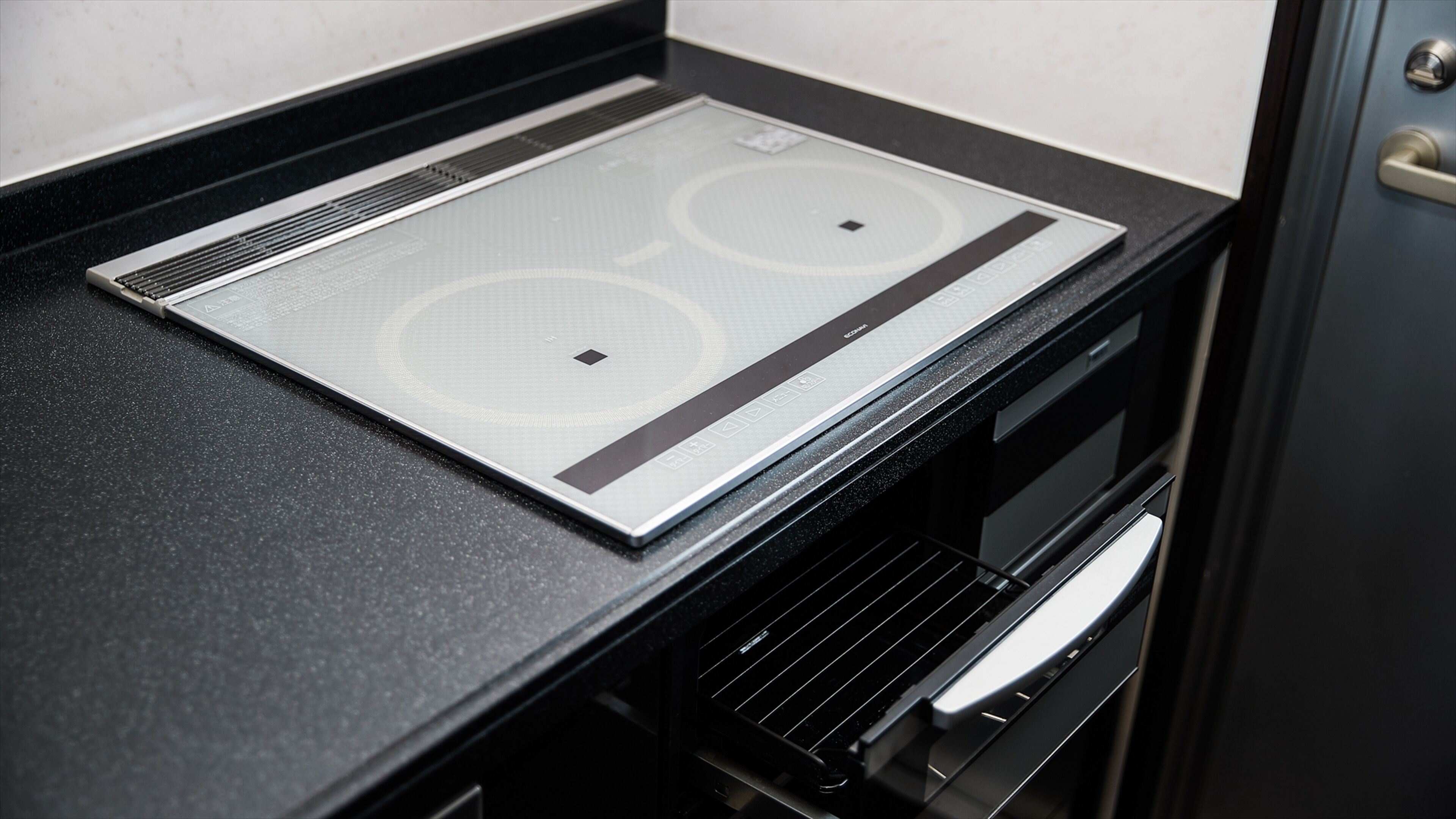 Uma cozinha com bancada preta, fogão embutido com painel de controle digital e forno de aço inoxidável.