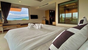 Quarto de hotel com uma cama grande, televisão, vista para o mar e varanda.