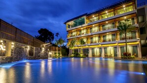 Um hotel com vários andares, piscina, área de estar externa e fachada bem iluminada.