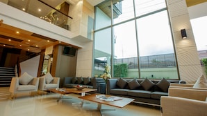 Uma sala de estar ampla com design moderno, apresentando um sofá grande, poltronas e uma mesa de centro. Uma escada leva a um andar superior, e amplas janelas proporcionam muita luz natural.