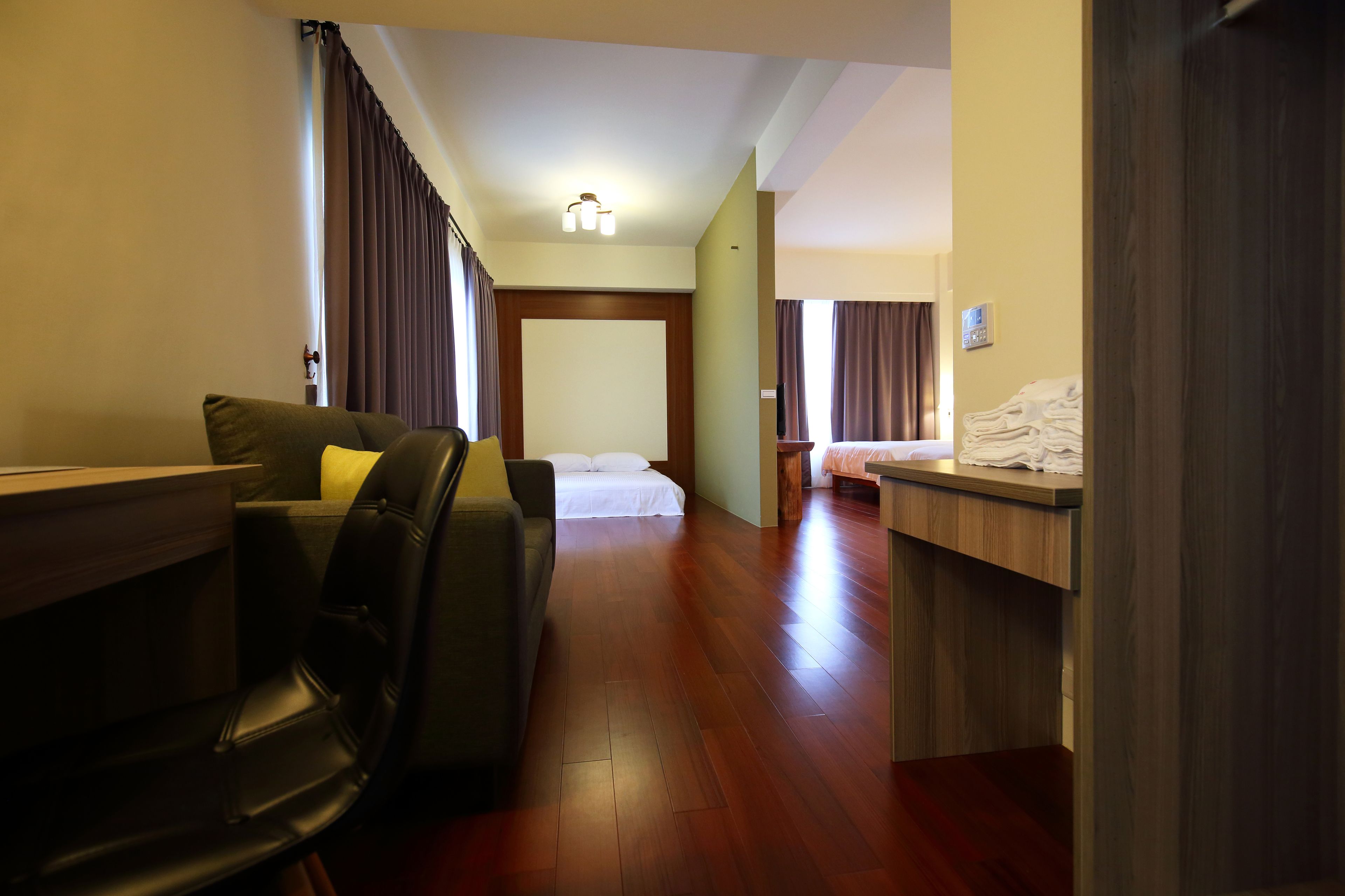 Quarto de hotel com piso de madeira, uma escrivaninha, um sofá, uma cama e banheiro com toalhas.