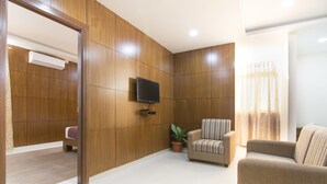 Uma sala de estar moderna com paredes de painel de madeira, uma televisão de tela plana na parede, dois sofás, um vaso de planta e uma porta deslizante que dá para outro cômodo.