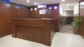 Uma mesa de recepção com uma placa que diz "Shaba", relógios e um vaso de planta.