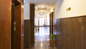 Um corredor com piso de mármore, painéis de madeira no teto e plantas em vasos ao longo das paredes.