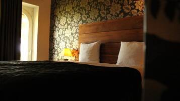 Quarto de hotel com cama, mesa de cabeceira e luminária, além de papel de parede floral.
