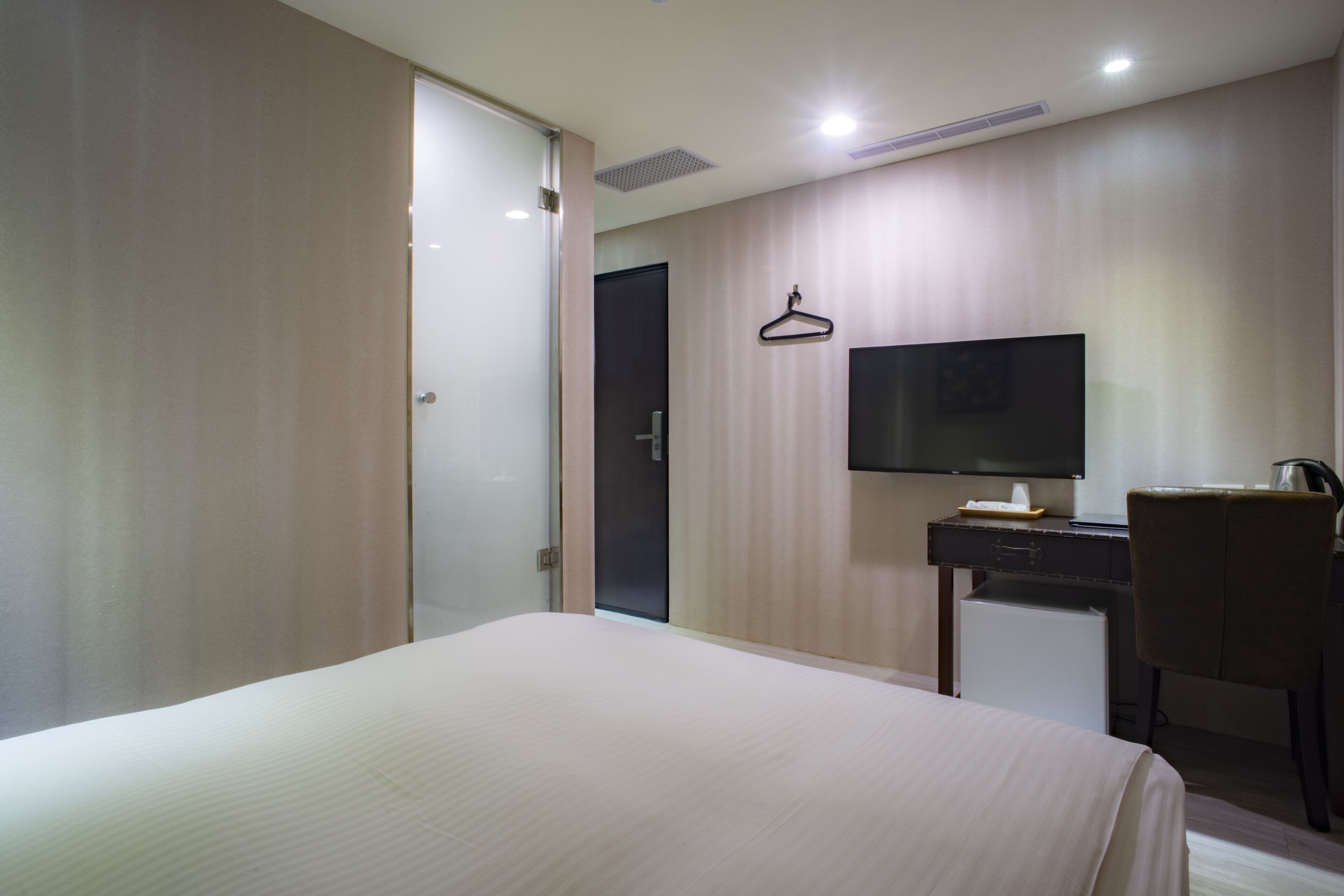 Quarto de hotel com cama, escrivaninha, cadeira, televisão e guarda-roupa.