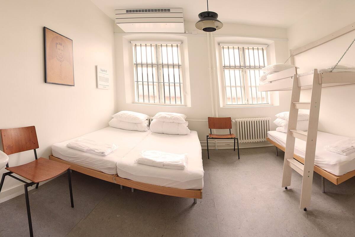 Um quarto de dormitório com beliches, uma mesa, uma cadeira e um radiador.