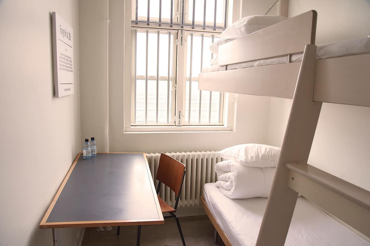 Quarto com beliche, mesa, cadeira, janela com grades e radiador.