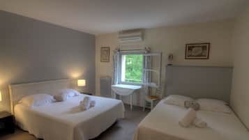 Quarto de hotel com duas camas, uma mesinha e uma janela com vista para o verde.