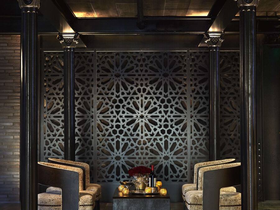 Um hall decorado com papel de parede estampado, dois poltronas, uma mesa de centro com bebidas e um objeto decorativo.