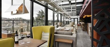 Um restaurante moderno com terraço, grandes janelas e vista para a cidade.