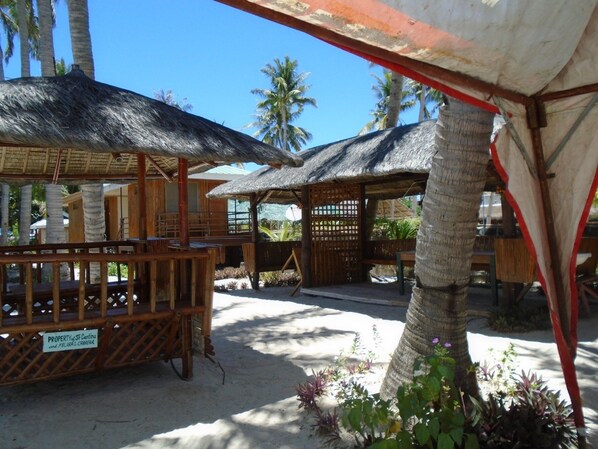 Um resort à beira-mar com cabanas de telhado de palha, móveis de madeira e palmeiras.
