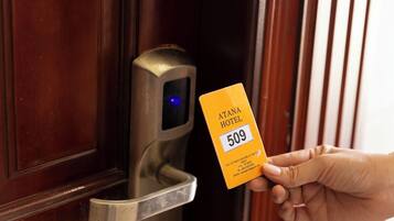 Mão segurando um cartão-chave de hotel com 'ATANA HOTEL' e o número do quarto '509' visíveis.