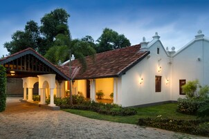 Um edifício branco com telhado em telhas vermelhas, um espaço coberto com colunas e uma entrada pavimentada.