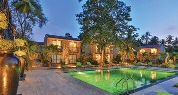 Hotel com piscina, espreguiçadeiras e área externa bem iluminada ao entardecer.
