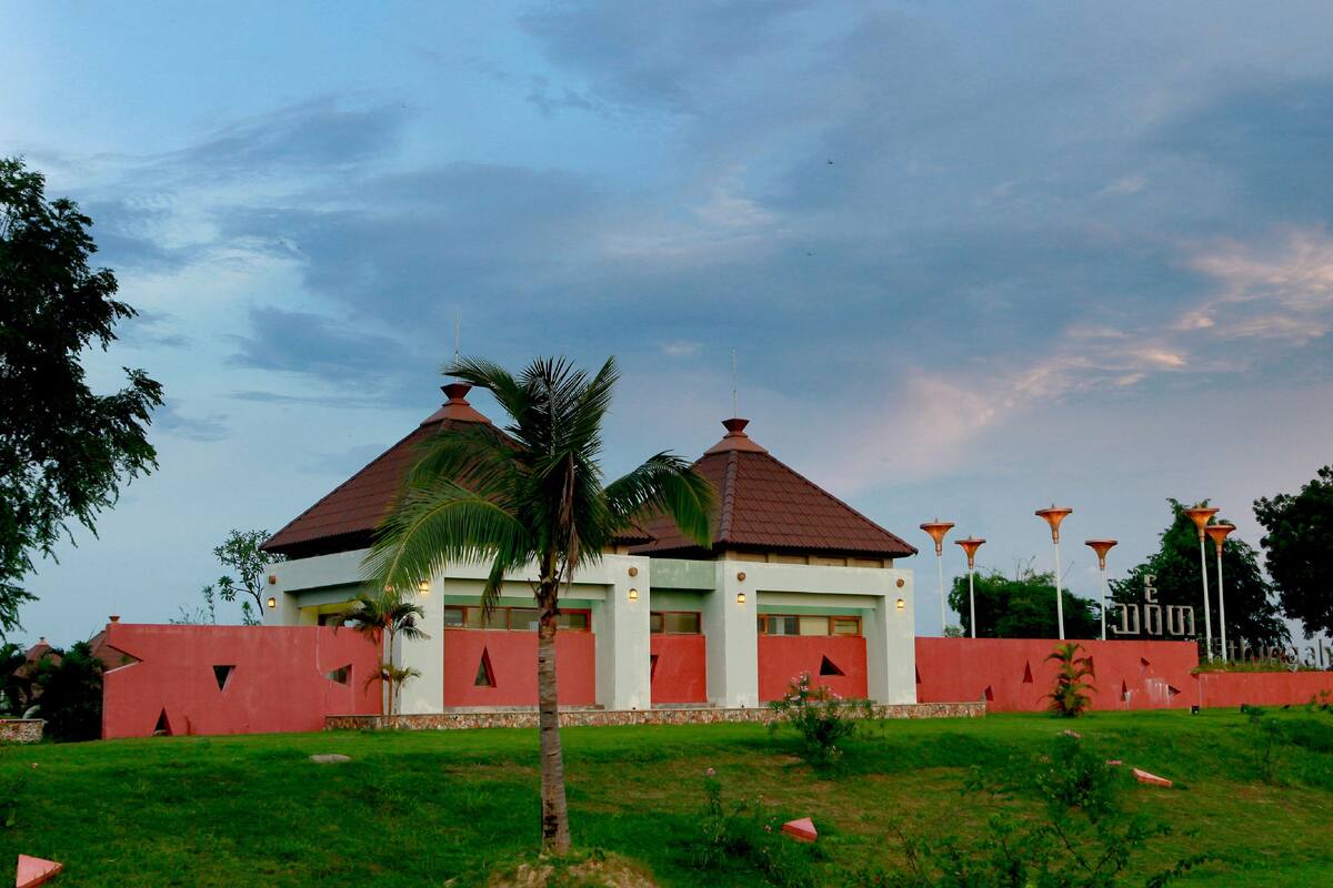 Um edifício com telhado vermelho e paredes brancas, rodeado por vegetação e palmeiras.