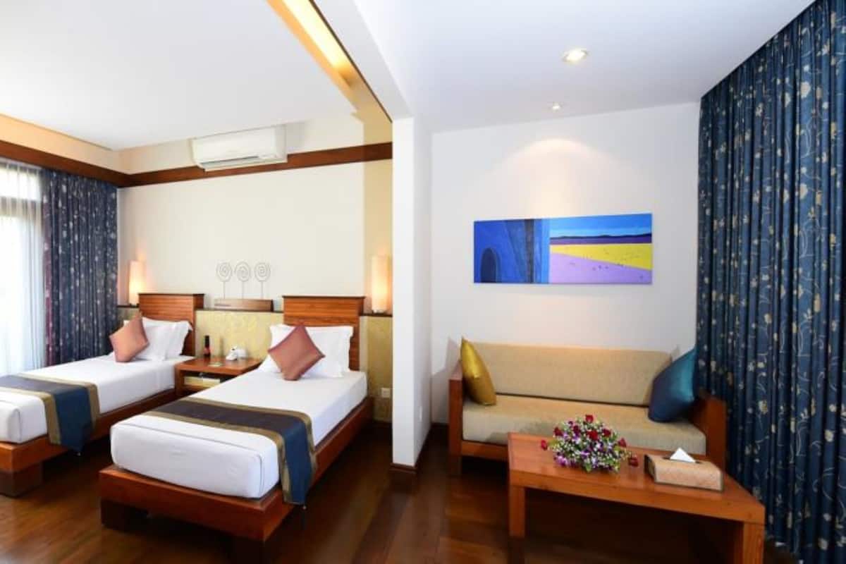 Quarto de hotel com duas camas, um sofá, uma mesa de centro e um quadro na parede.