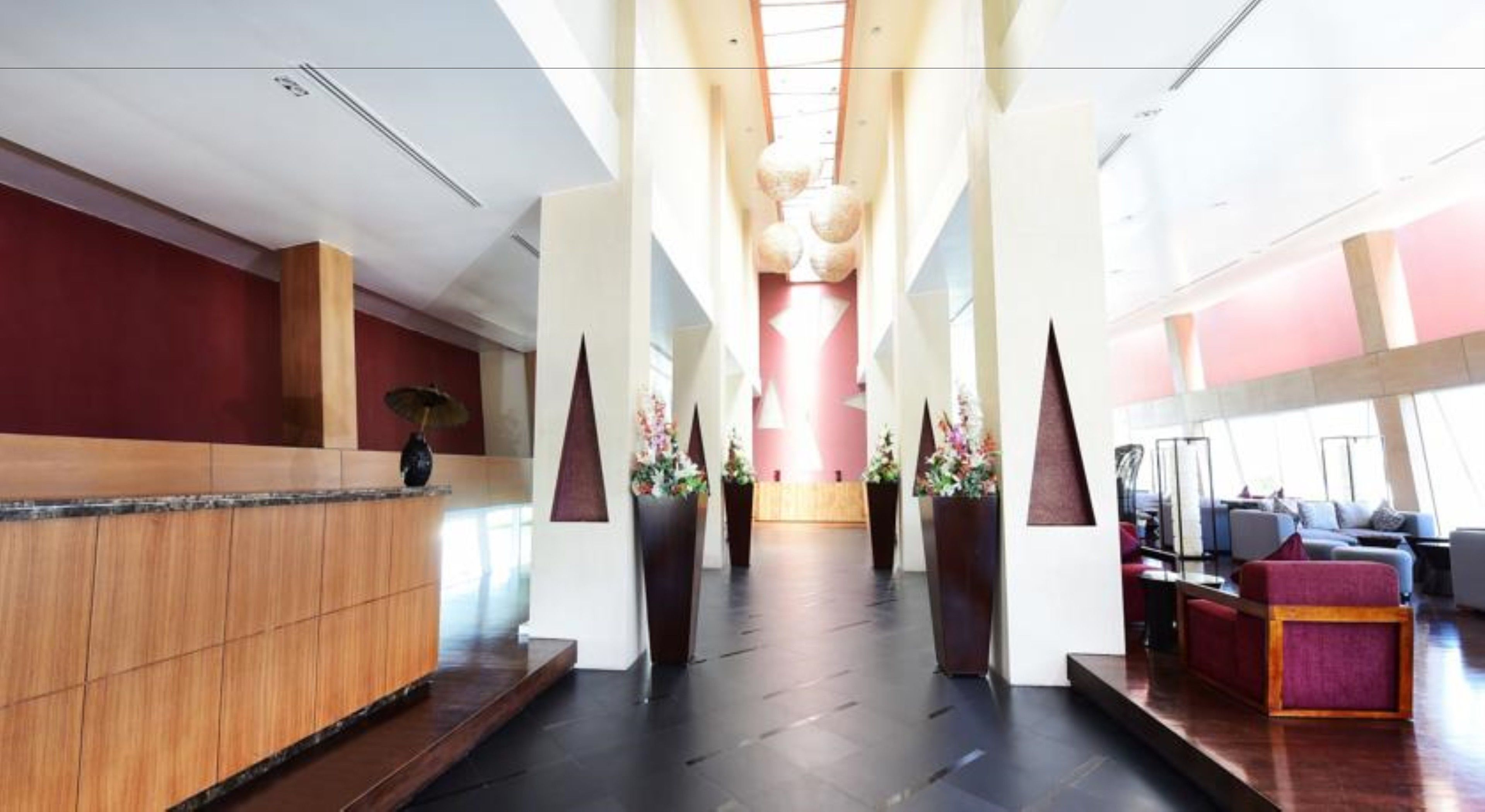 Um lobby moderno de hotel com balcão de recepção, área de estar e plantas decorativas.