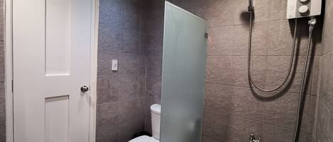 Casa de banho com sanita branca, cabine de duche em vidro e painel de comando fixado à parede.