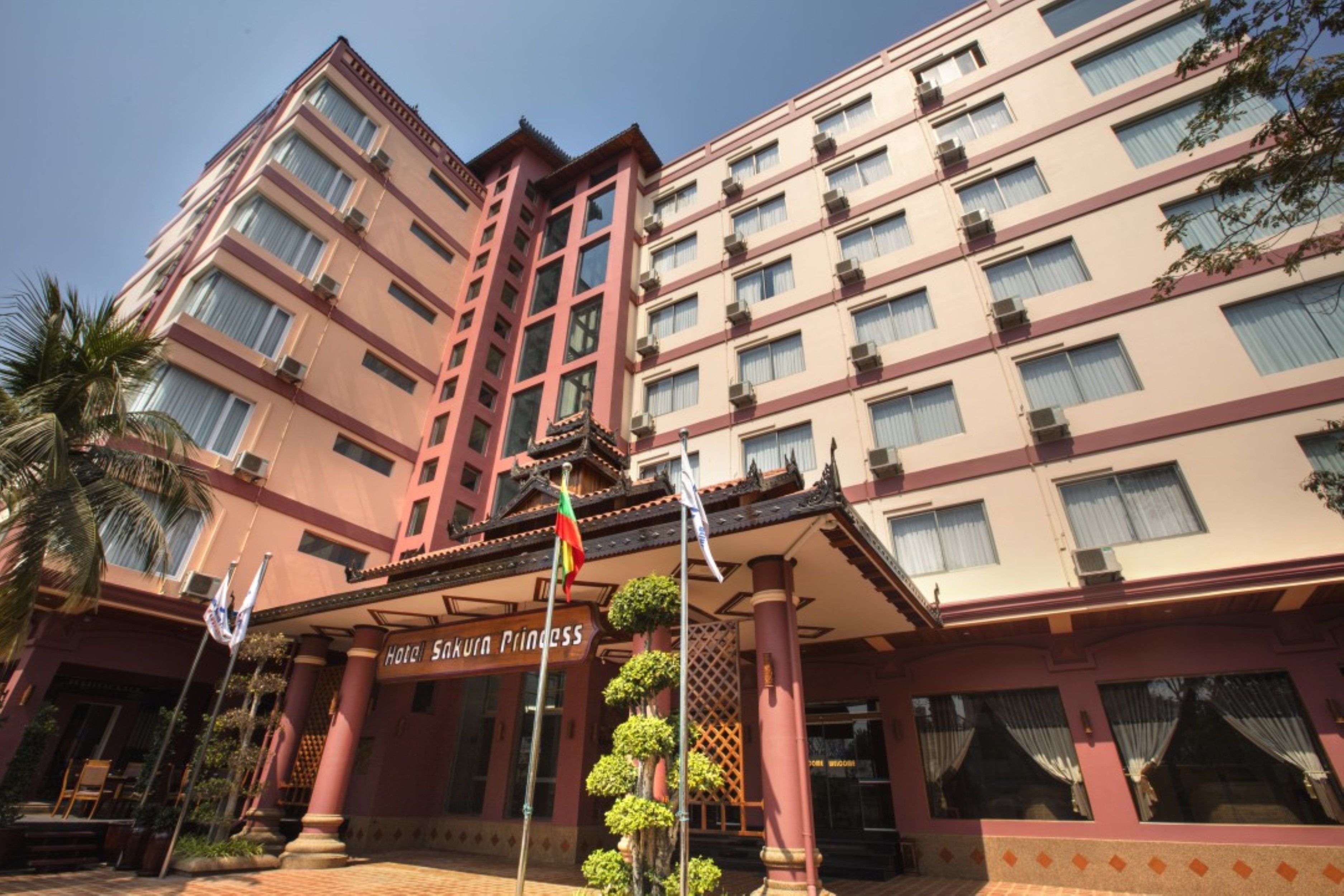 Um hotel de vários andares com estilo arquitetônico tradicional, apresentando uma entrada imponente com uma placa indicando "Hotel Sakura Princess".
