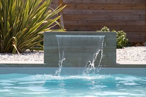 Piscina com cascata, cercada por uma vedação de madeira e vegetação.