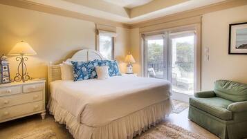 Quarto com cama, duas mesas de cabeceira, uma poltrona verde e varanda com vista.