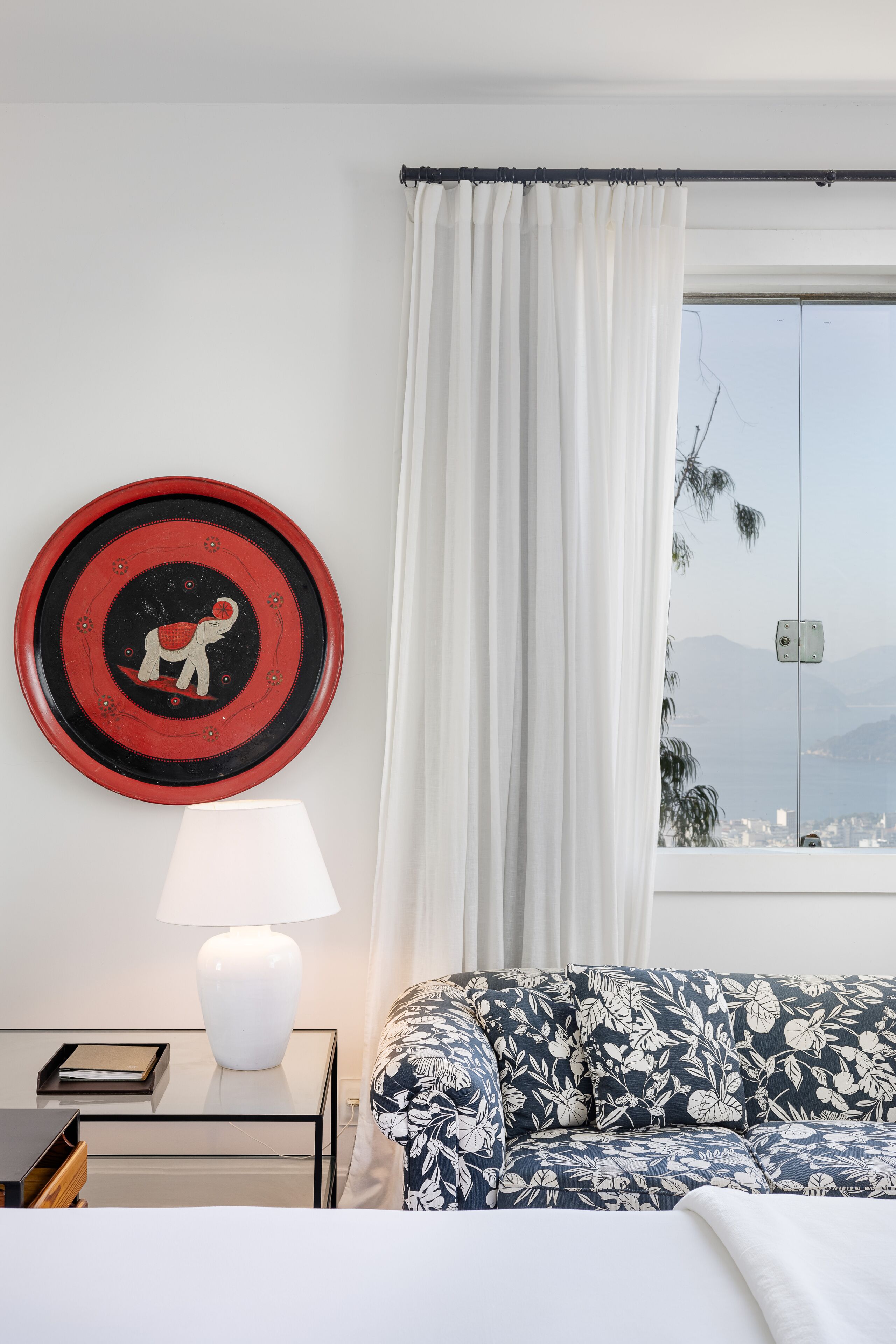 Quarto de hotel com uma cama, uma mesa de cabeceira com luminária, uma obra de arte na parede e uma janela com vista para as montanhas.