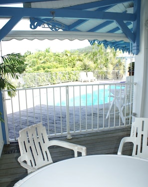 Uma área externa coberta com piscina, cadeiras brancas e um deck de madeira.