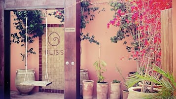 Área de chuveiro com regadera, cadeira balanço, plantas em vasos e uma placa com a inscrição