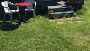 Um pequeno edifício térreo com porta branca e um pequeno alpendre. Há uma mesa e duas cadeiras do lado de fora.