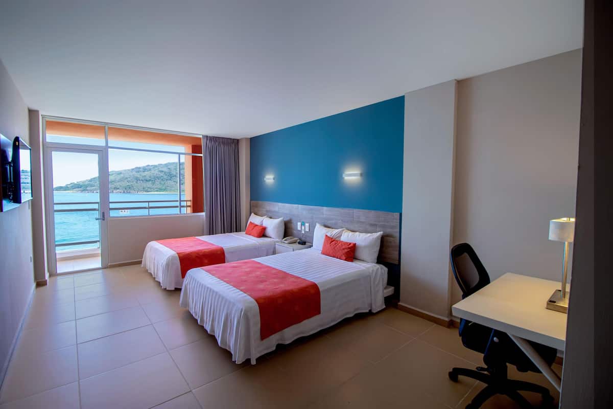 Quarto de hotel com duas camas, uma escrivaninha, uma cadeira, uma televisão e vista para o mar.