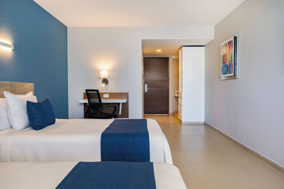 Quarto de hotel com duas camas, uma escrivaninha e uma cadeira.