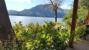 Um jardim com vista para um lago, um deck de madeira e montanhas ao fundo.