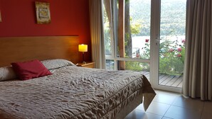 Quarto de hotel com uma cama, mesa de cabeceira, abajur e vista para uma varanda florida.