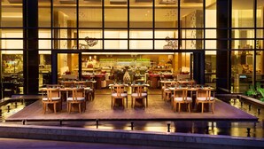 Um restaurante com área externa, janelas amplas e um espelho d'água à frente.