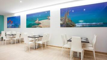 Uma sala de conferências com cadeiras e mesas brancas, três grandes quadros com paisagens costeiras e uma parede de destaque azul-esverdeado.