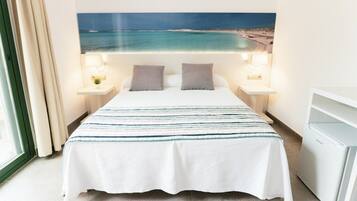 Quarto de hotel com cama, duas luminárias de cabeceira, mesa de apoio, vista para o mar e janela com cortinas.