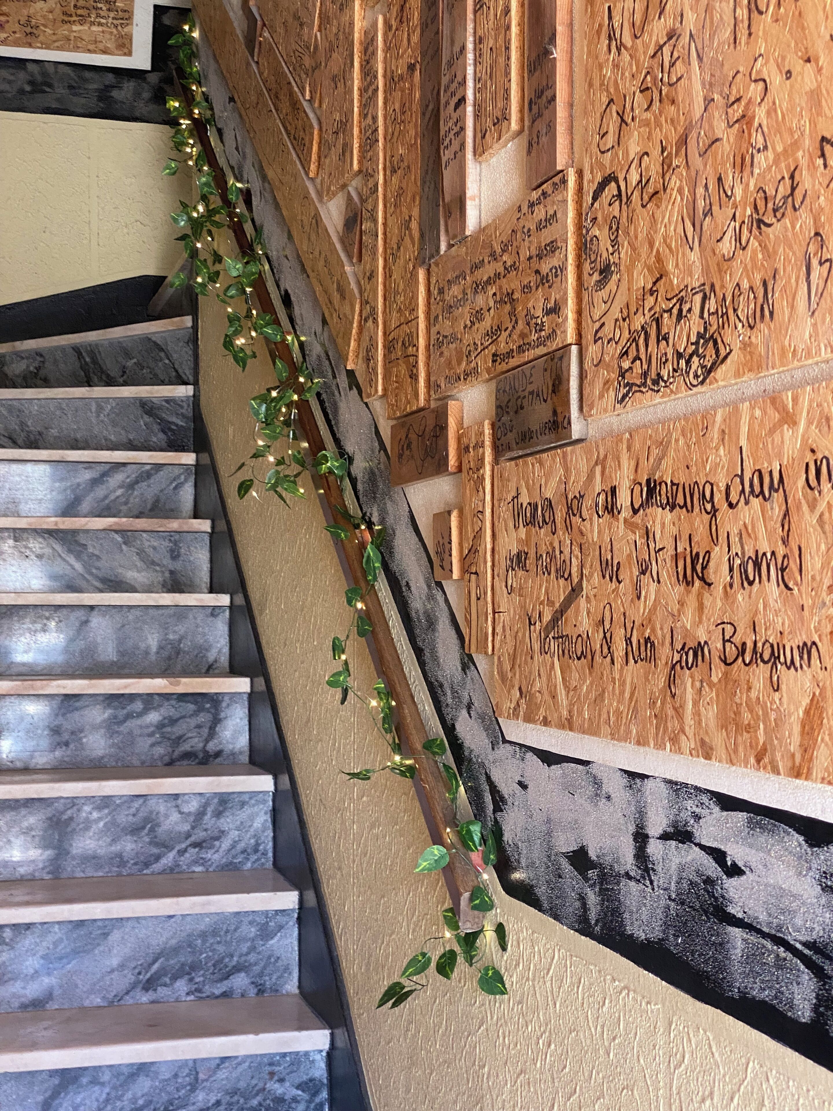 Uma escadaria com parede de madeira decorada com mensagens escritas à mão e uma guirlanda de luzes.