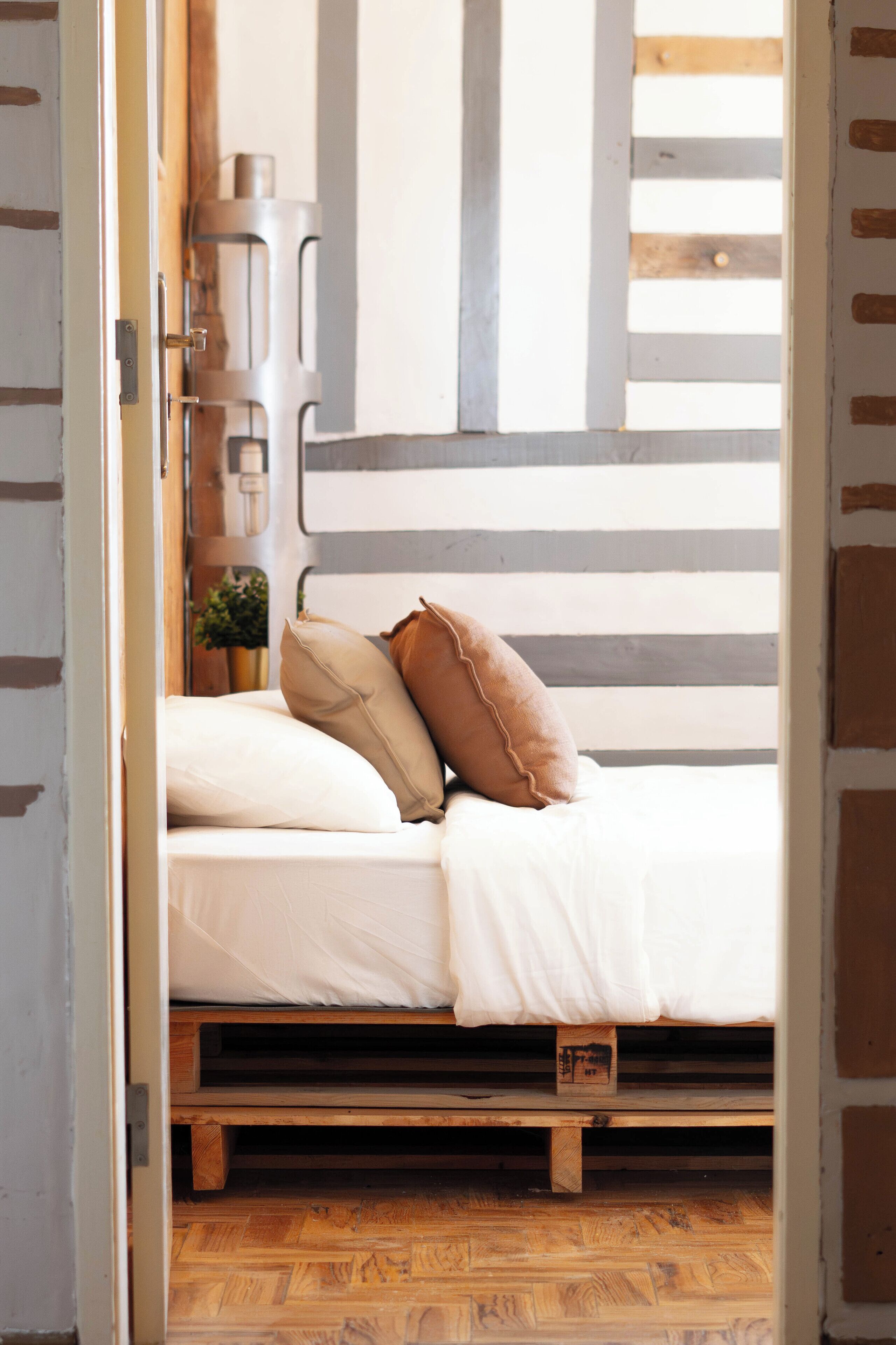 Cama com estrutura de madeira, roupa de cama branca e travesseiro marrom.